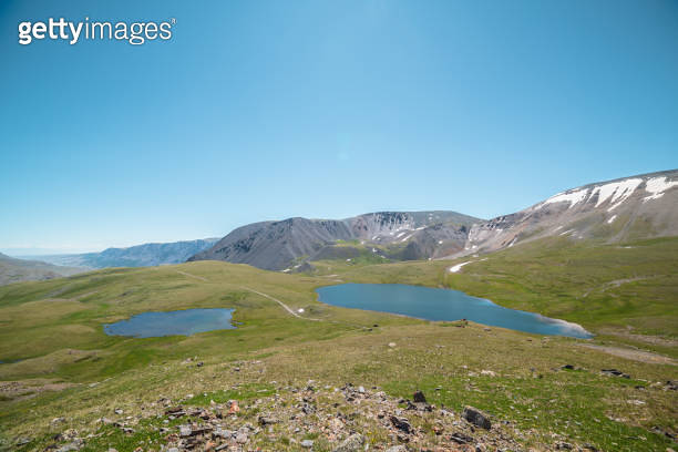 Two lakes, sunlit green meadow, alpine valley and mountain range. Blue ...