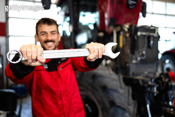 Happy caucasian serviceman holding wrench tool ready to repair tractor ...
