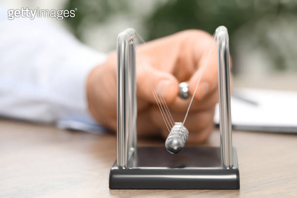 Man playing with Newton's cradle at table, closeup. Physics law of ...