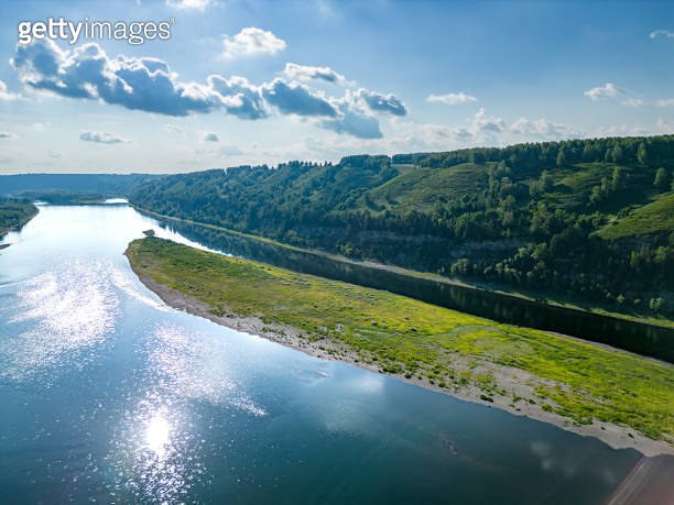 an island in the middle of a flat river whose high bank is overgrown ...