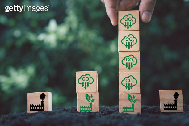 Hand stacking CO2 reducing icon on green factory for decrease CO2 , carbon footprint and carbon ...