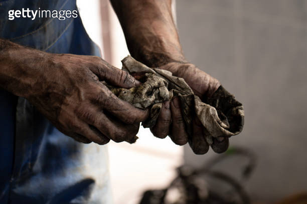 A male auto mechanic repairs a car and wipes his dirty hands on a rag ...