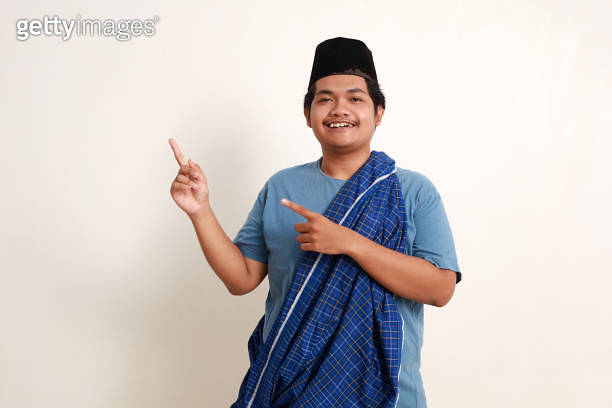 Smiling young asian muslim boy standing while pointing sideways ...