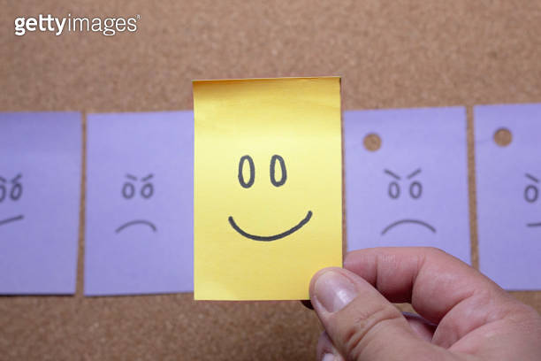 A person holding a yellow sticky note with a happy face in front of a ...