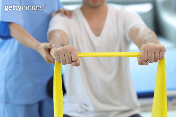 Nurse doing physiotherapy arm to male patient using elastic band in ...