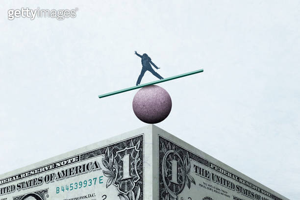 Woman Struggles To Balance At Corner Of Dollar Bill (2092257857) - 게티이미지뱅크