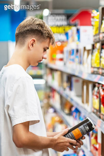 Focused thoughtful young guy choosing food in supermarket, holding jars ...