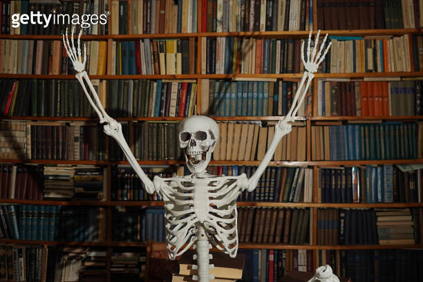 Human skeleton with arms raised up. Bookshelves with books. (2162545561 ...