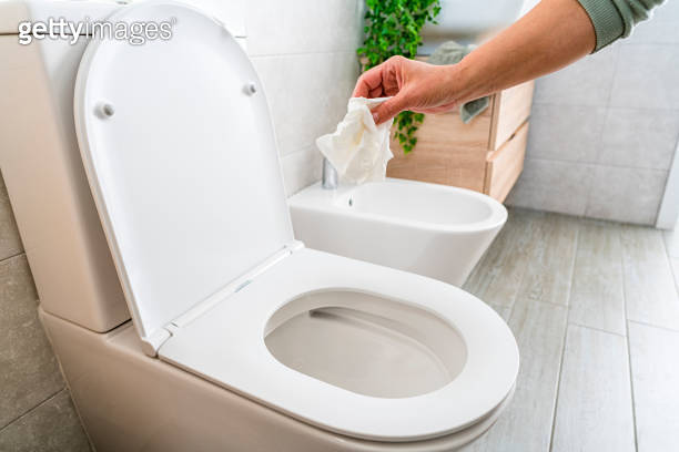 Close up of woman hand throwing toilet paper in the toilet bowl ...
