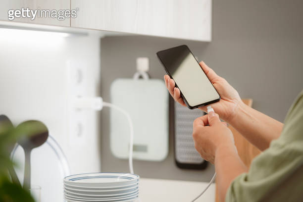 Woman in kitchen plugging mobile phone battery charger cable 이미지 ...
