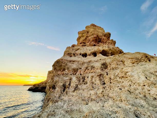 Towering limestone cliffs with lots of caves rise up from a stormy sea ...