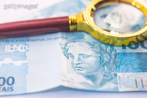 Brazilian Real 100 reais notes and a magnifying glass in the ...