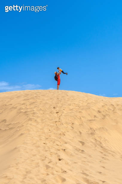 Mother lifting child smiling in the dunes of Maspalomas on vacation ...