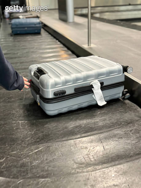 Close-up image of unrecognisable woman collecting wheelie luggage from ...