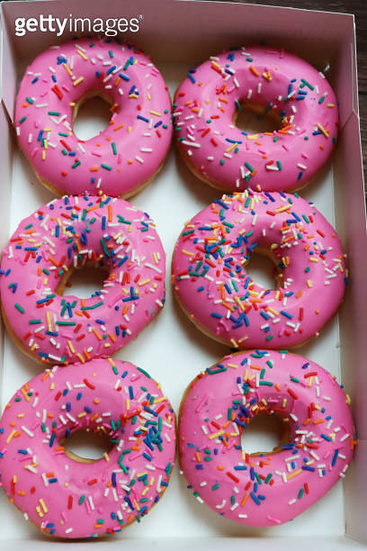 Full frame image of cardboard box of pink fondant iced ring doughnuts ...