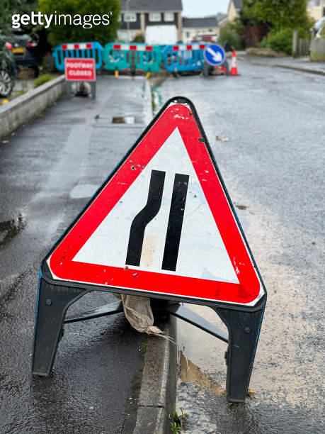 Close-up image of road narrows on left ahead sign with sandbag ...