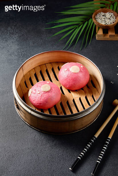 Pink bao buns shaped like pigs in a bamboo steamer; a playful and ...