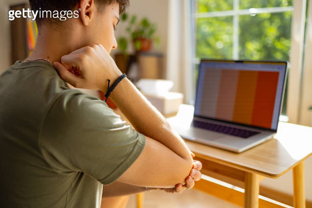 Male high school student experiencing a pain in elbow, while e-learning ...