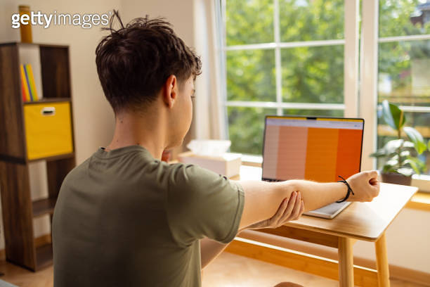 Male high school student experiencing a pain in elbow, while e-learning ...