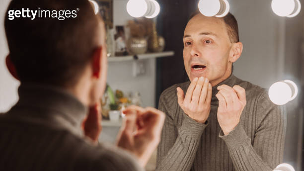 Metrosexual mid-adult man applying an face cream while observing ...