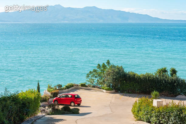 Red car on the road near the ocean on sunny summer day. Red car parked ...
