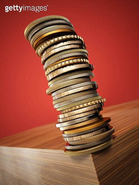 Precarious Stack of Various Coins Teetering on Wooden Surface Against ...