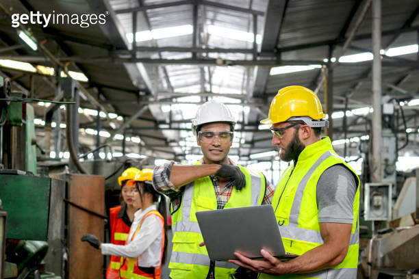 Industrial foreman and worker with helmet and safety vest using laptop ...