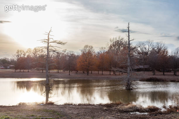 Sun breaking through clouds over small lake with fall colors and trees ...