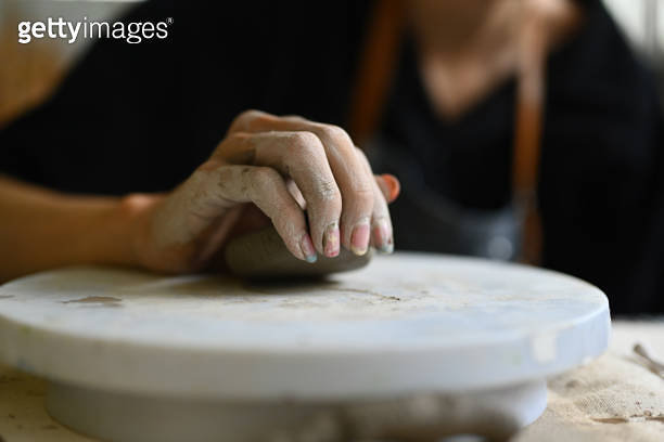 A close-up of Artisan's hands forming pieces of a small clay on a ...