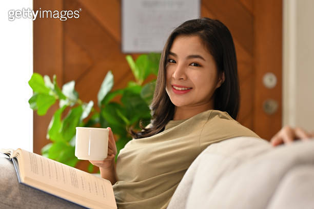 Attractive young Asian woman enjoying reading a book while relaxing in ...