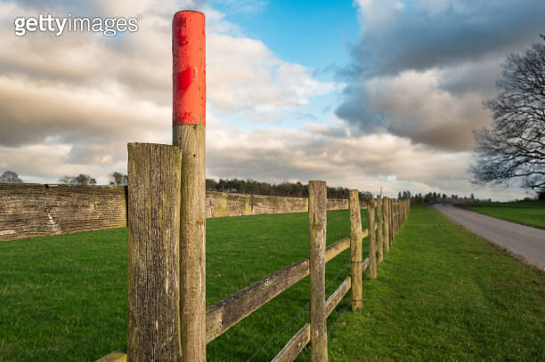 Shallow focus of a red painted post seen along a wooden arable farm ...