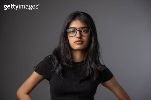 Young Indian girl with glasses standing in front of a grey background ...