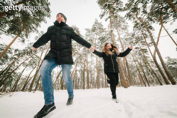 Man and woman running in snow in winter forest. Happy winter holidays ...