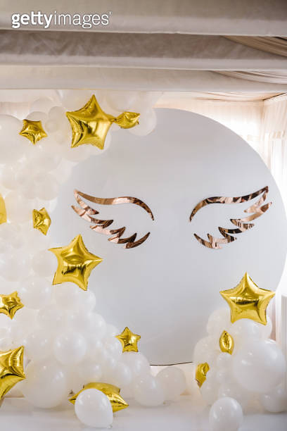 Arch decorated white, golden balloons in the shape of stars, and angel wings for a baptism party ...