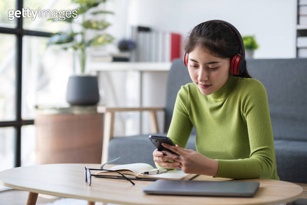 Asian woman using smartphone while working with headphones in modern ...