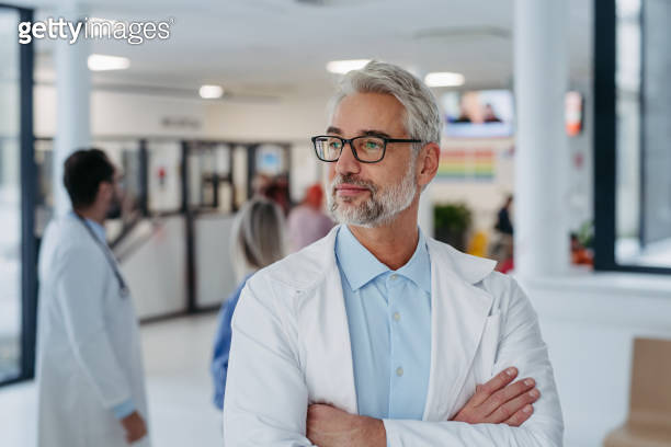 Portrait of confident mature doctor standing in Hospital corridor ...