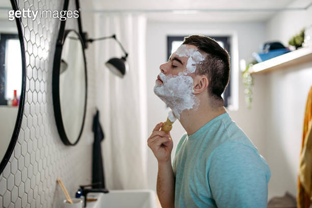 Young man with down syndrome learning how to shave, applying shaving foam all over his face ...