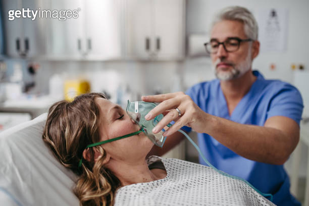 Doctor putting oxygen mask on patient face. Male nurse taking care of ...