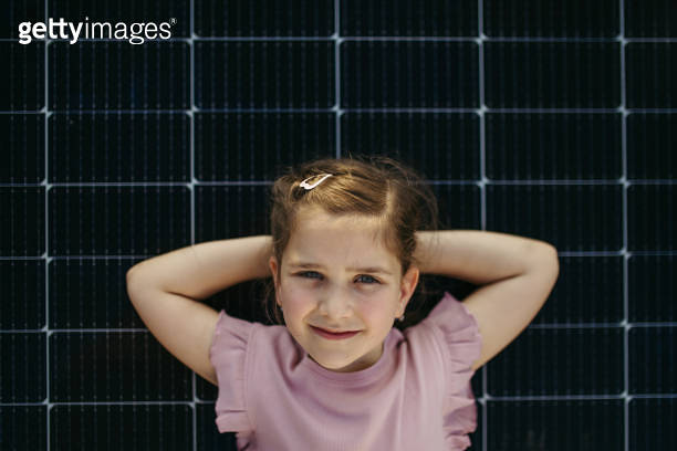 Top view of girl lying on solar panels roof, looking at camera. Rooftop ...