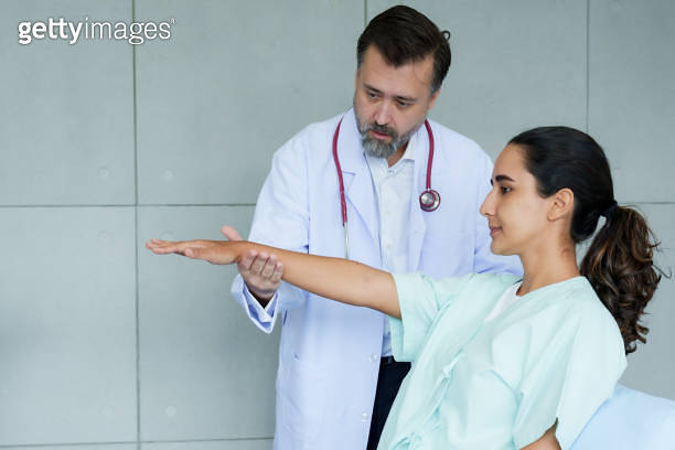 physiotherapist examines the extended arm of a female patient, focusing ...