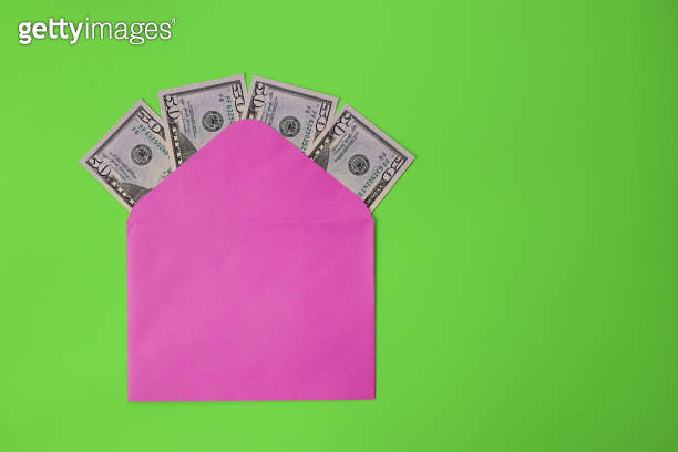 A pink envelope full of fifty dollar bills isolated on a lime green ...