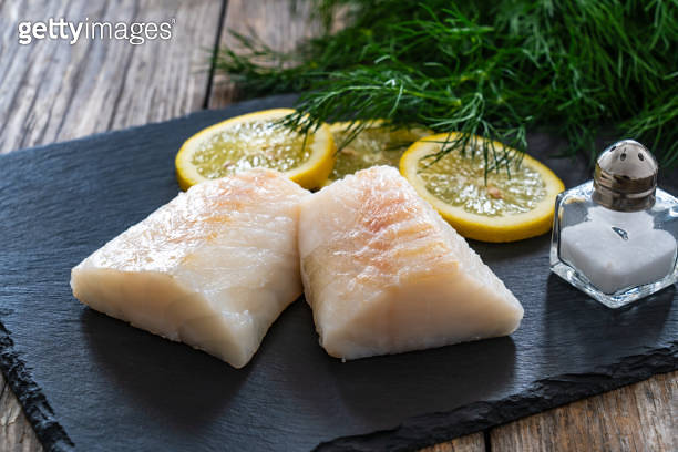Fresh raw codfish fillet with lemon and dill on black stony cutting ...
