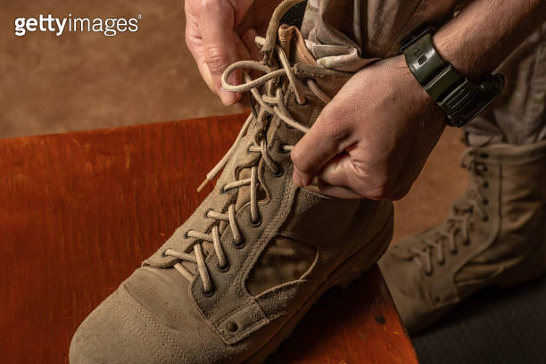 Close-up of man's hands tying laces of military boots. Beige suede army ...
