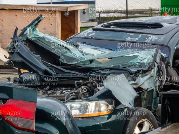 A severely damaged car, with a crumpled hood and shattered windshield ...