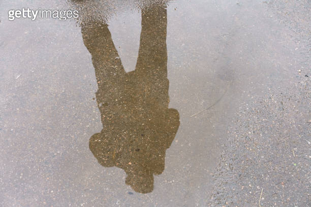 Person's shadow is cast on the ground in a puddle (2187660686) - 게티이미지뱅크