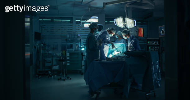 Diverse Surgical Team Working in a Darkened Operating Room Surrounded ...