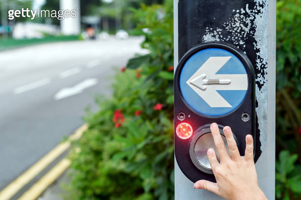 A child hand presses a pedestrian crossing button with a glowing ...